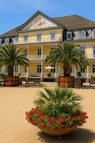 Hotel de vários andares com varandas, palmeiras e um pátio de areia.