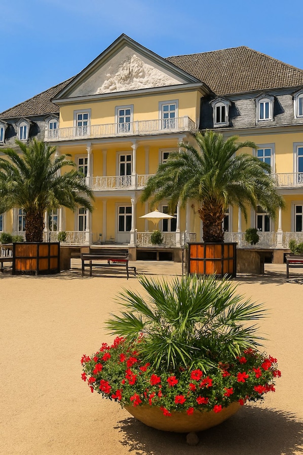 Hotel de vários andares com varandas, palmeiras e um pátio de areia.