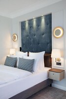 Quarto de hotel com uma cama grande, duas mesas de cabeceira e luminária fixada na parede.