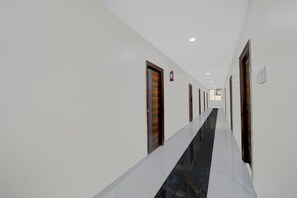 Um corredor comprido e estreito, com paredes brancas e chão de piso de mármore preto e branco.