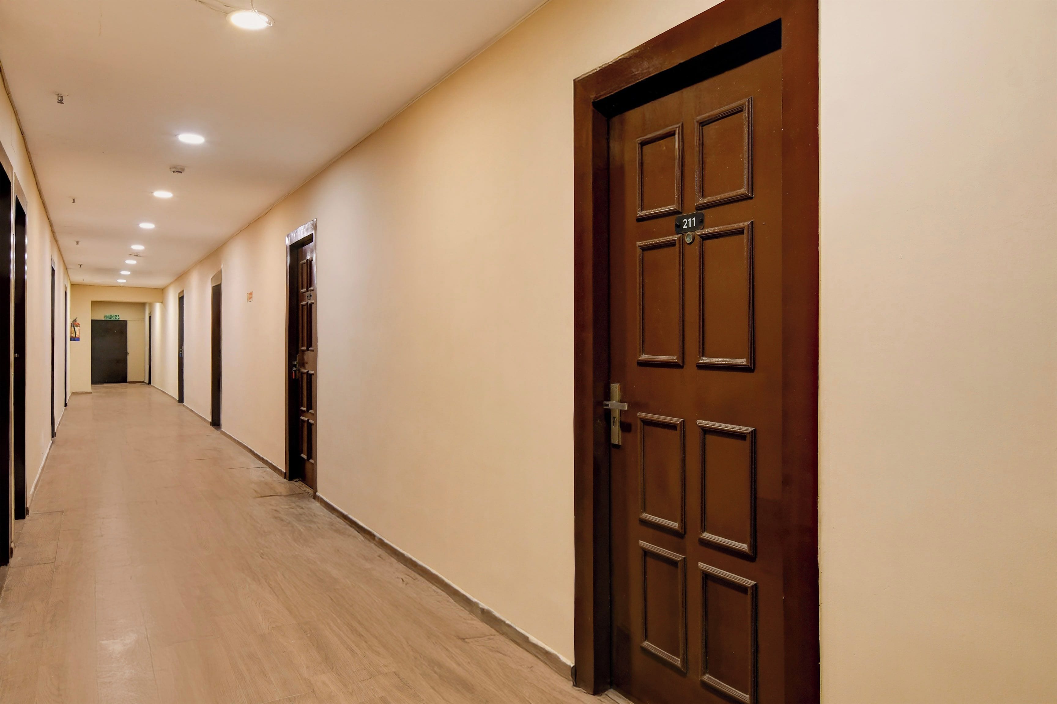 Corredor de hotel com portas de madeira, piso de madeira e luminárias embutidas no teto.