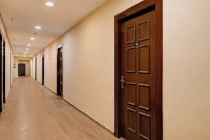 Corredor de hotel com portas de madeira, piso de madeira e luminárias embutidas no teto.