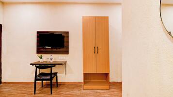 Quarto com guarda-roupa de madeira, televisão na parede, mesa pequena com cadeira e planta em vaso.