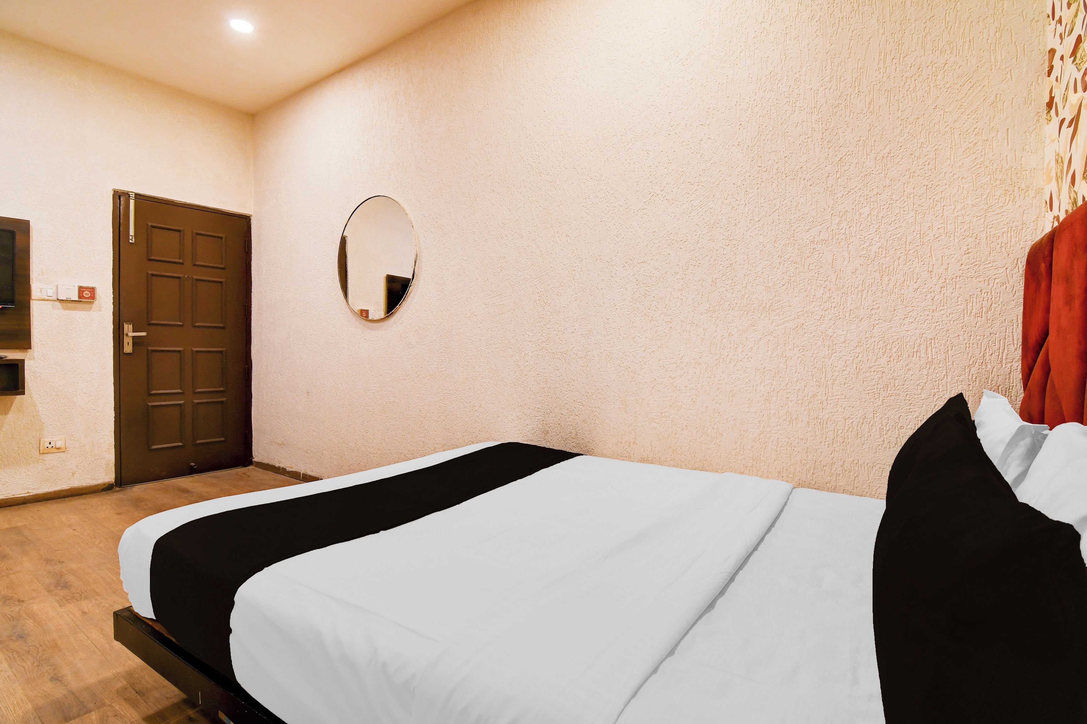 Quarto de hotel com cama, porta, espelho fixado na parede e interruptor de luz.