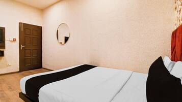 Quarto de hotel com cama, porta, espelho fixado na parede e interruptor de luz.