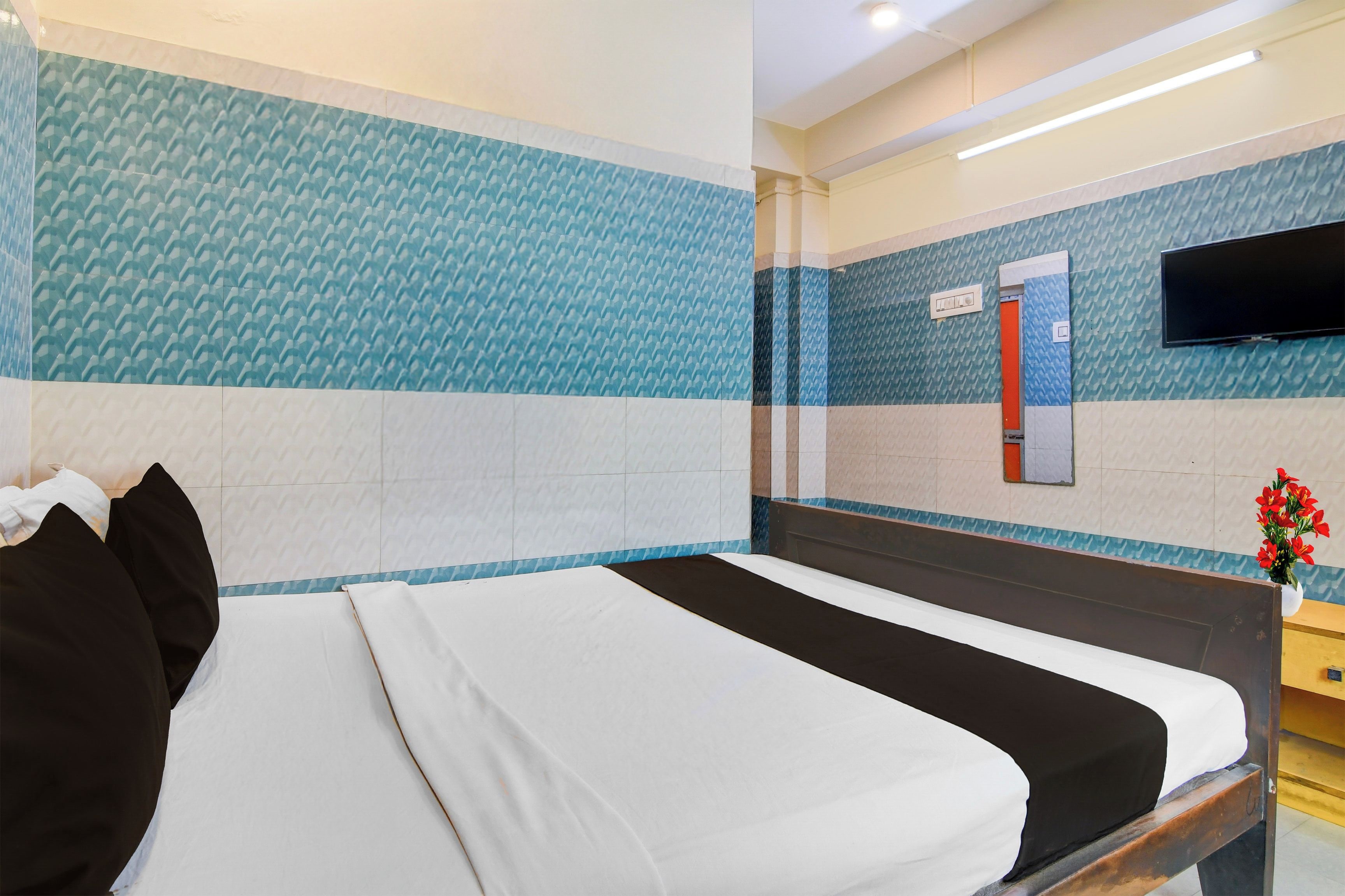 Quarto de hotel com uma cama, televisão de tela plana, mesa pequena e um vaso com flores.