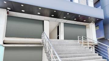 Escadaria que leva a um edifício com portões fechados, grades de metal e design moderno.