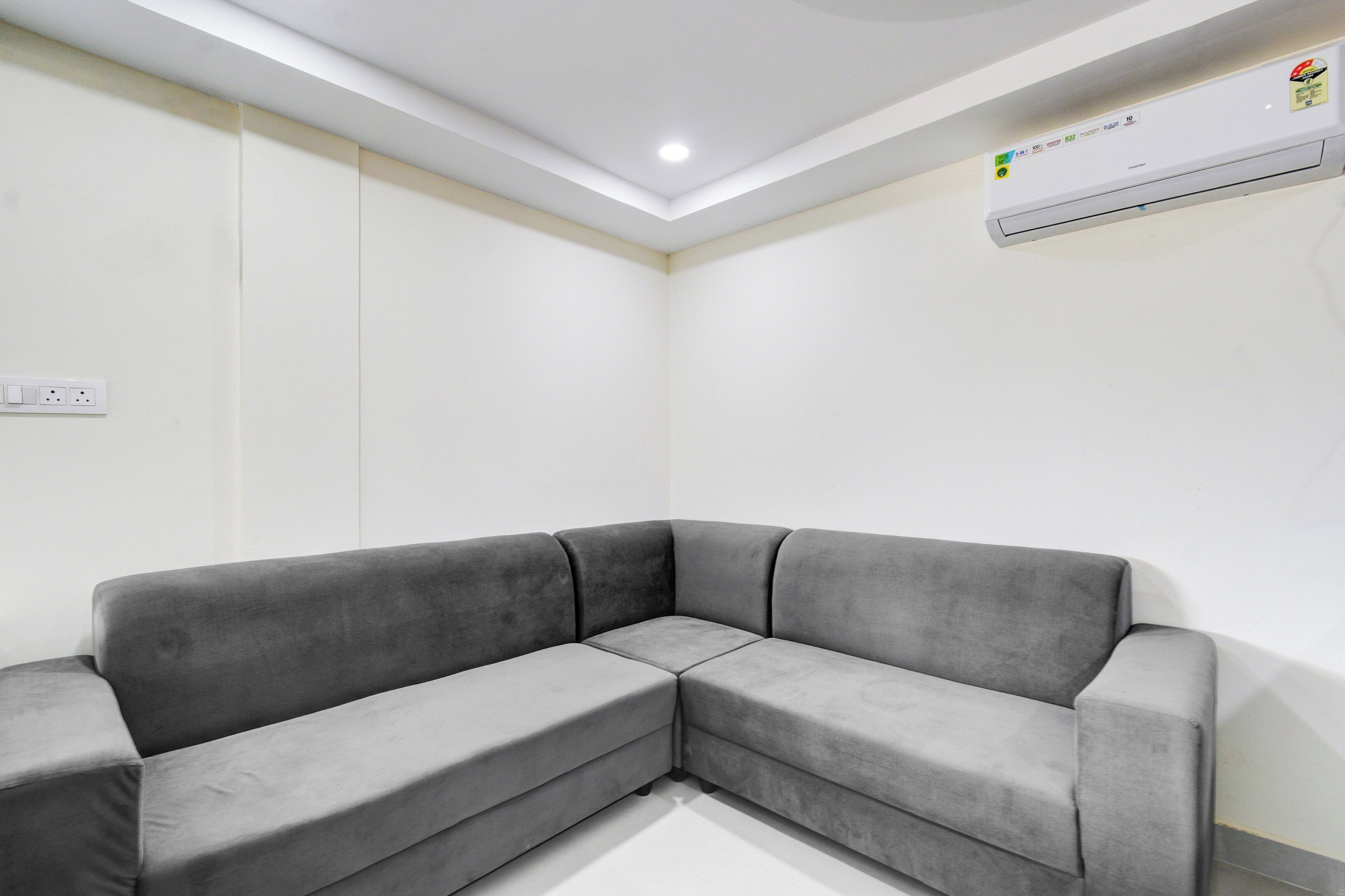 Quarto de canto com sofá seccional cinza, teto branco e aparelho de ar condicionado.