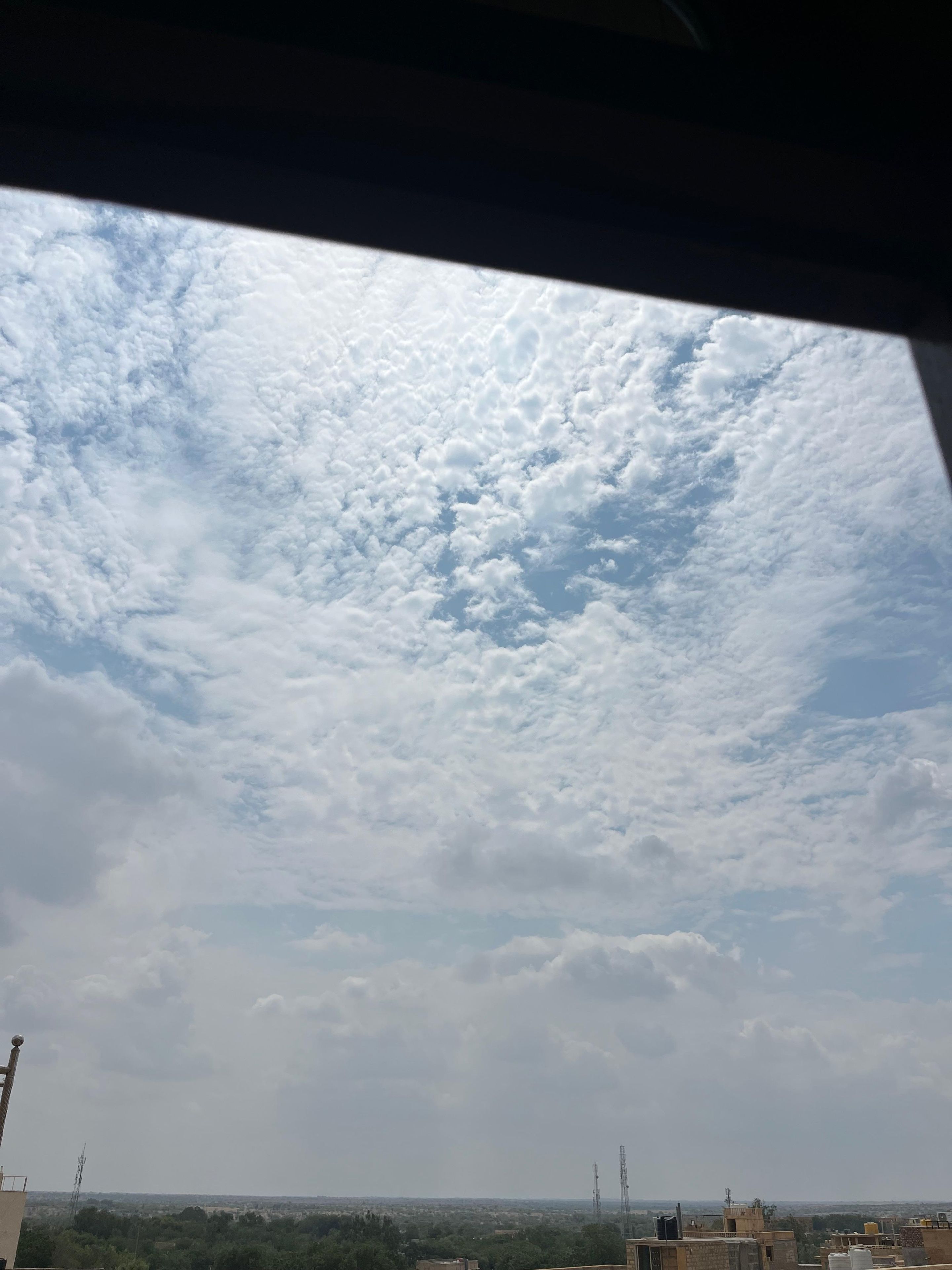 Vista de um céu nublado pela janela, com uma paisagem urbana repleta de edifícios e vegetação.