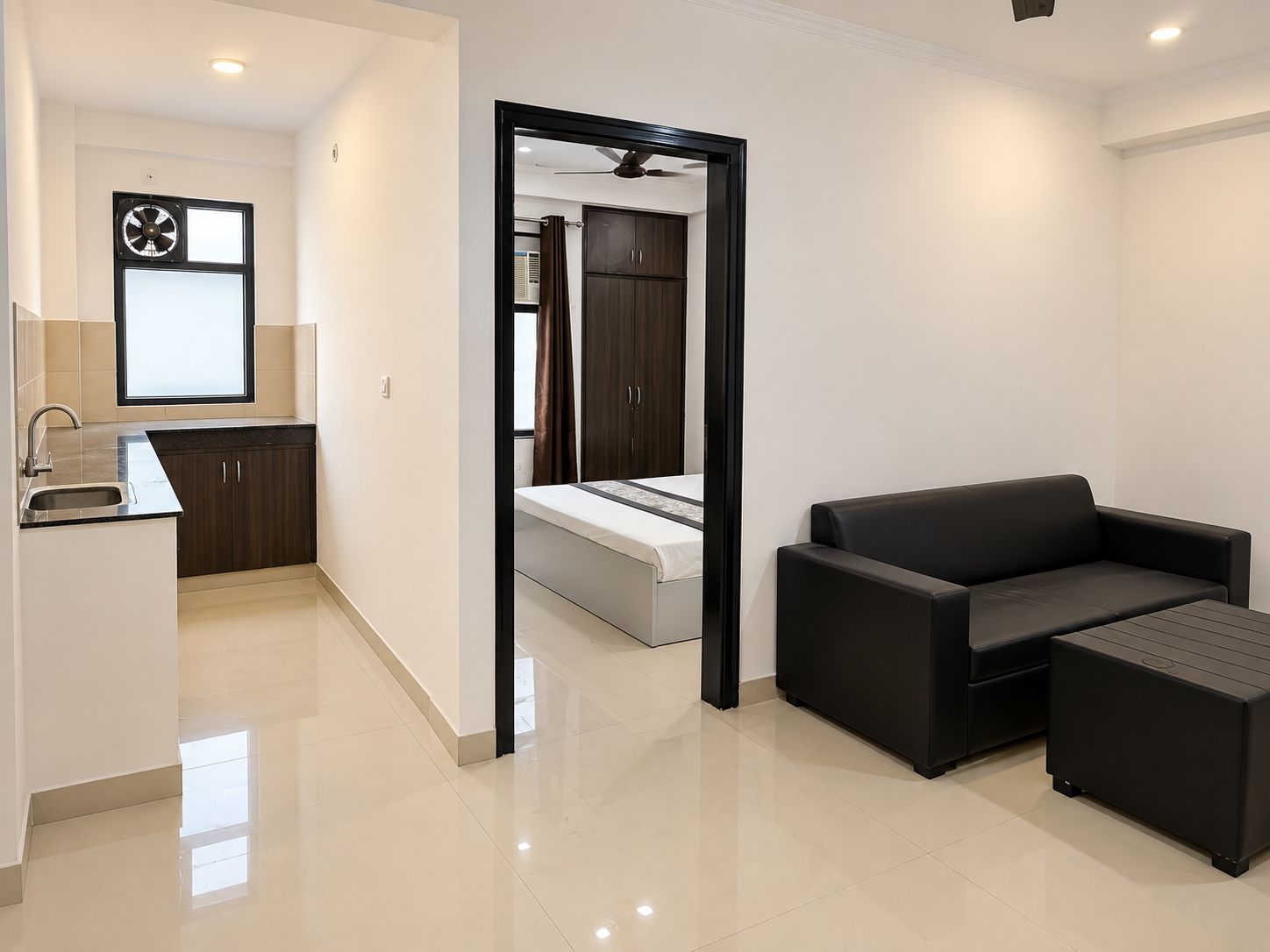 Uma sala de estar moderna com sofá e mesa de centro, uma cozinha com pia e armários, e uma porta de entrada para um quarto com cama e guarda-roupa.