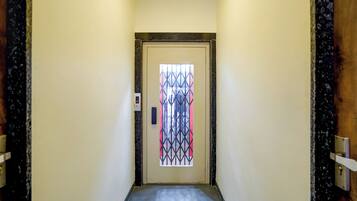 Um corredor com uma porta no final, um interruptor de luz na parede e uma câmera de segurança acima da porta.