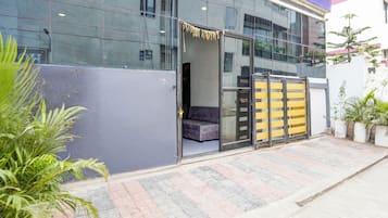 Edifício moderno com fachada de vidro, entrada com portão e calçada pavimentada.