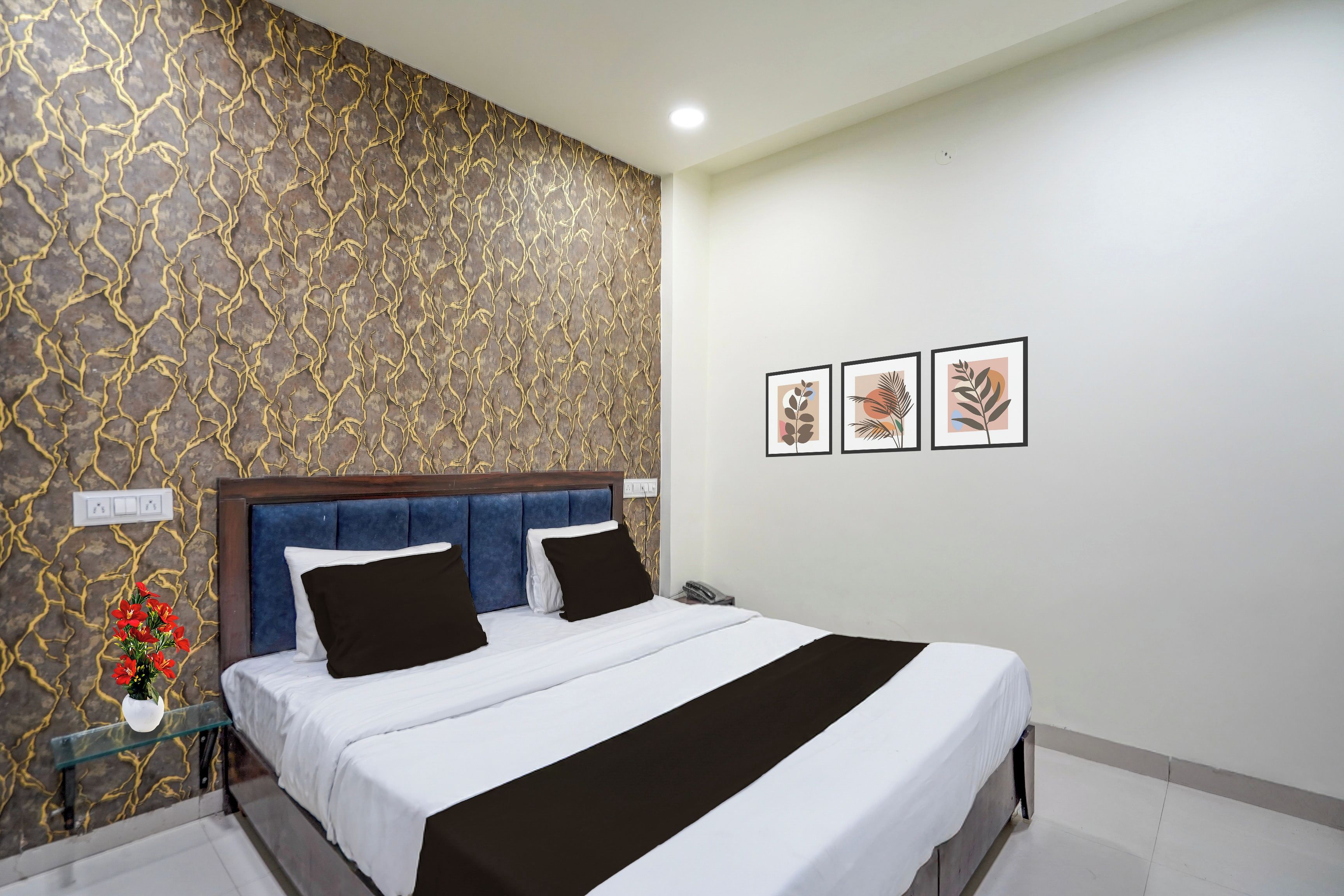 Quarto de hotel com cama, mesa de cabeceira, telefone fixado na parede e uma parede com três quadros.
