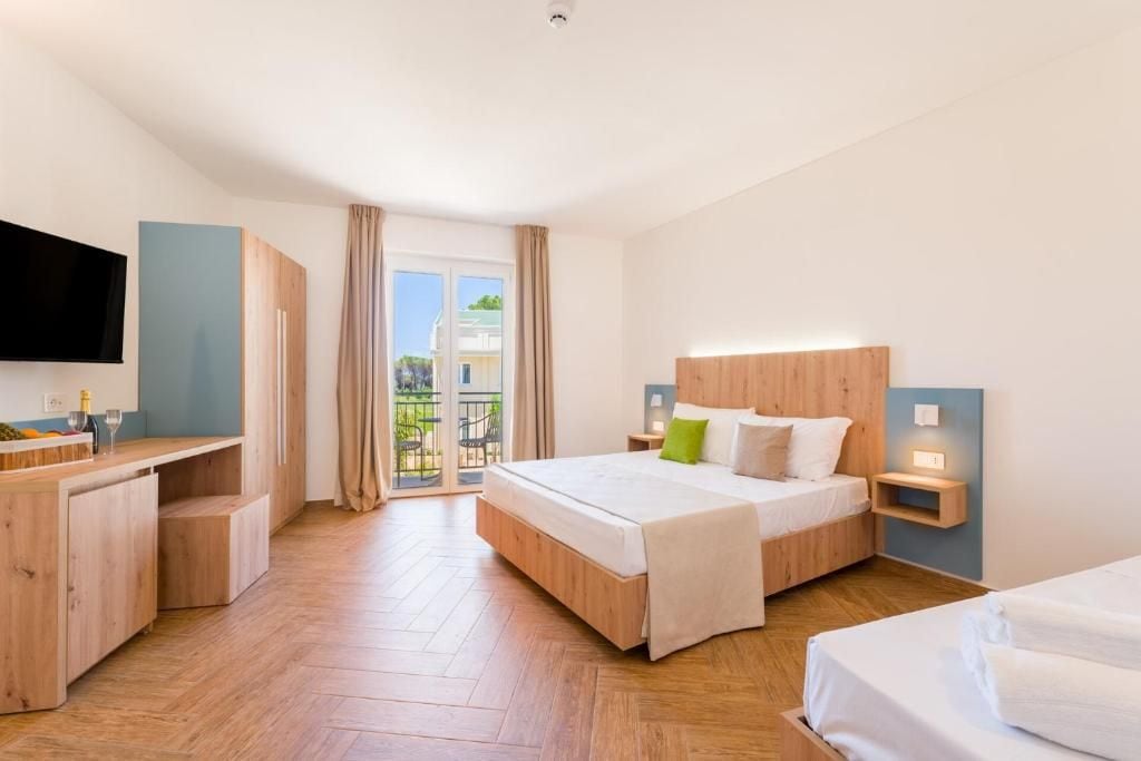 Quarto de hotel com cama, escrivaninha, televisão e varanda com cortinas.