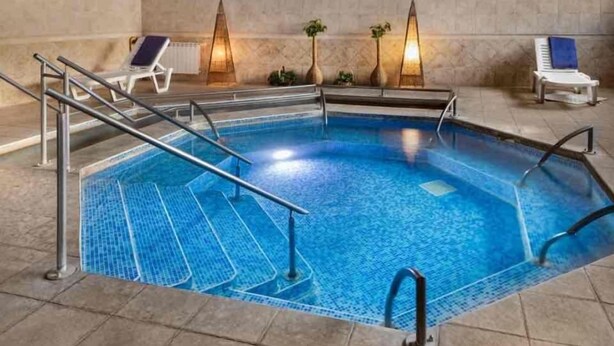Piscina com piso de azulejos, corrimãos de metal e espreguiçadeiras com toalhas.
