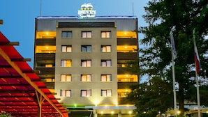 Entrada de hotel com escadaria que leva ao saguão, área externa coberta para descanso e um mastro.