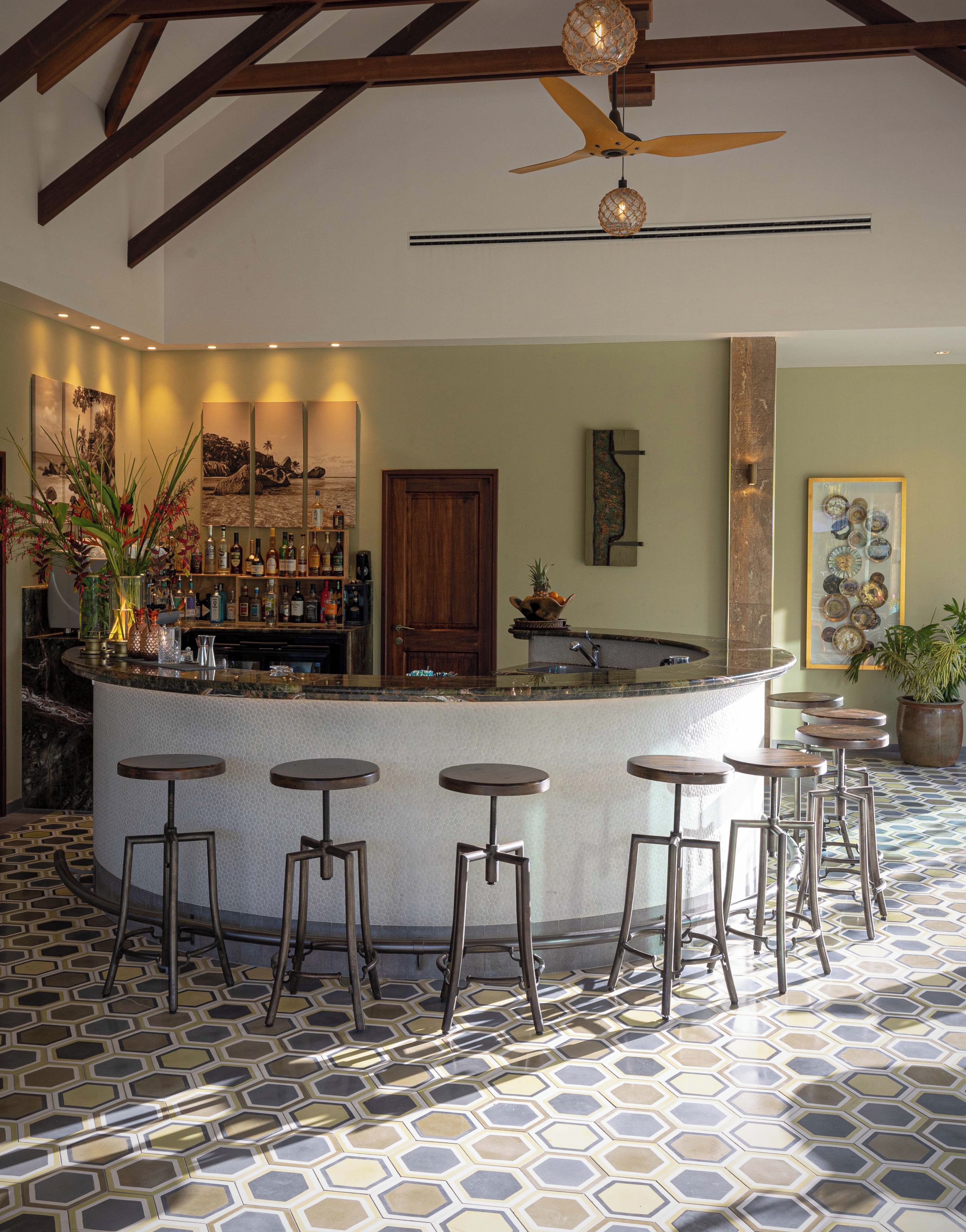 Uma área de bar com uma ilha central, banquetas e um ventilador de teto.