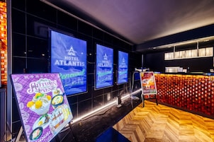 Um saguão de hotel com design moderno, apresentando um balcão de recepção, uma parede com várias telas exibindo a marca 'Hotel Atlantis' e um piso padronizado.