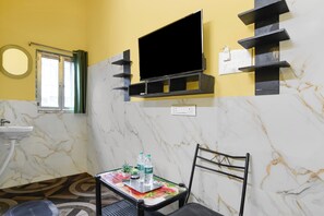 Quarto com televisão na parede, pia, janela e mesa com cadeira.