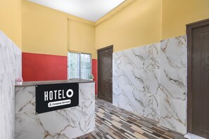 Uma área de recepção de hotel com balcão de mármore, parede com destaque em vermelho e piso estampado.
