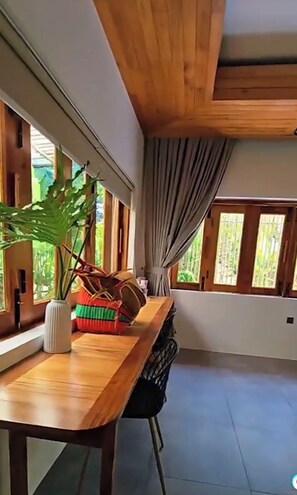 Uma área de refeições com mesa de madeira, cadeiras, planta em vaso e uma janela com cortinas.