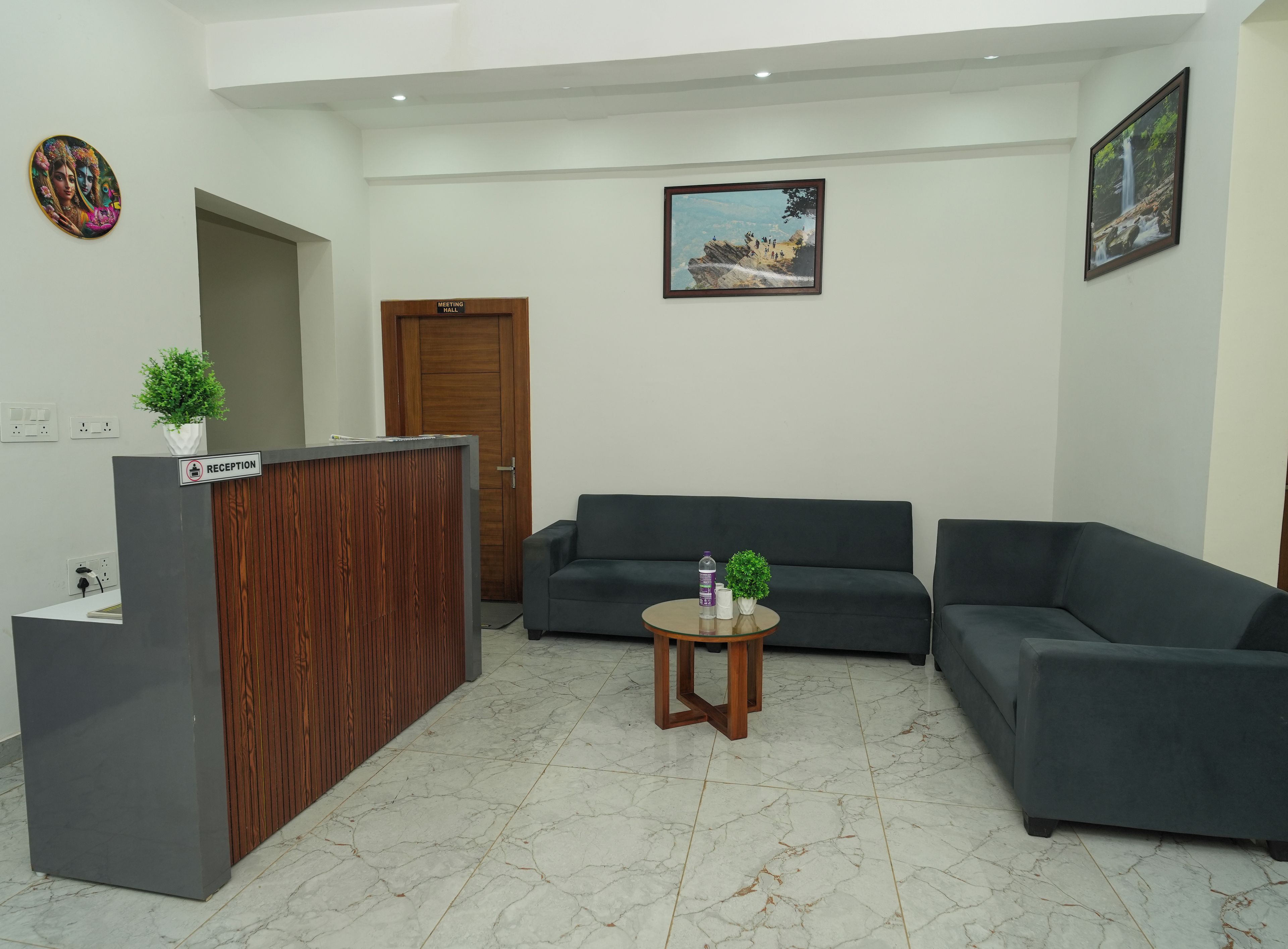 Uma área de recepção com balcão, sofá, uma mesa pequena e uma porta identificada como 'MEETING ROOM'.