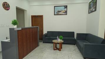 Uma área de recepção com balcão, sofá, uma mesa pequena e uma porta identificada como 'MEETING ROOM'.
