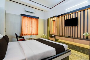 Quarto de hotel com cama, escrivaninha, cadeira, televisão e janela com cortinas.