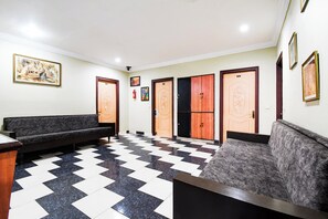 Um hall com piso xadrez, dois sofás e portas numeradas.