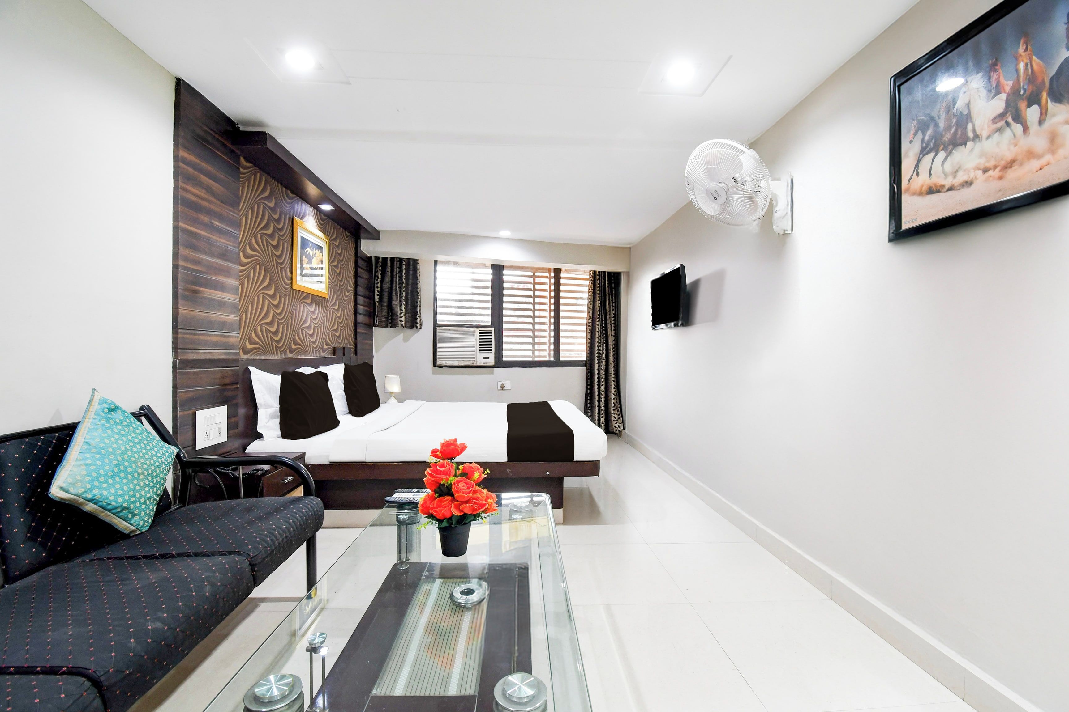Quarto de hotel moderno com cama, sofá, mesa de centro com um vaso de flores e um quadro na parede.