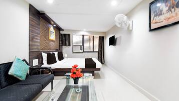 Quarto de hotel moderno com cama, sofá, mesa de centro com um vaso de flores e um quadro na parede.