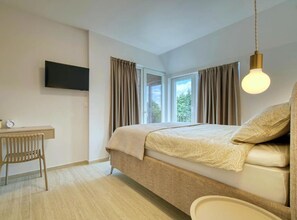 Quarto com cama, escrivaninha, cadeira, televisão e janela com cortinas.