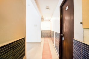 Corredor de hotel com porta de madeira, piso de azulejos e luminária na parede.