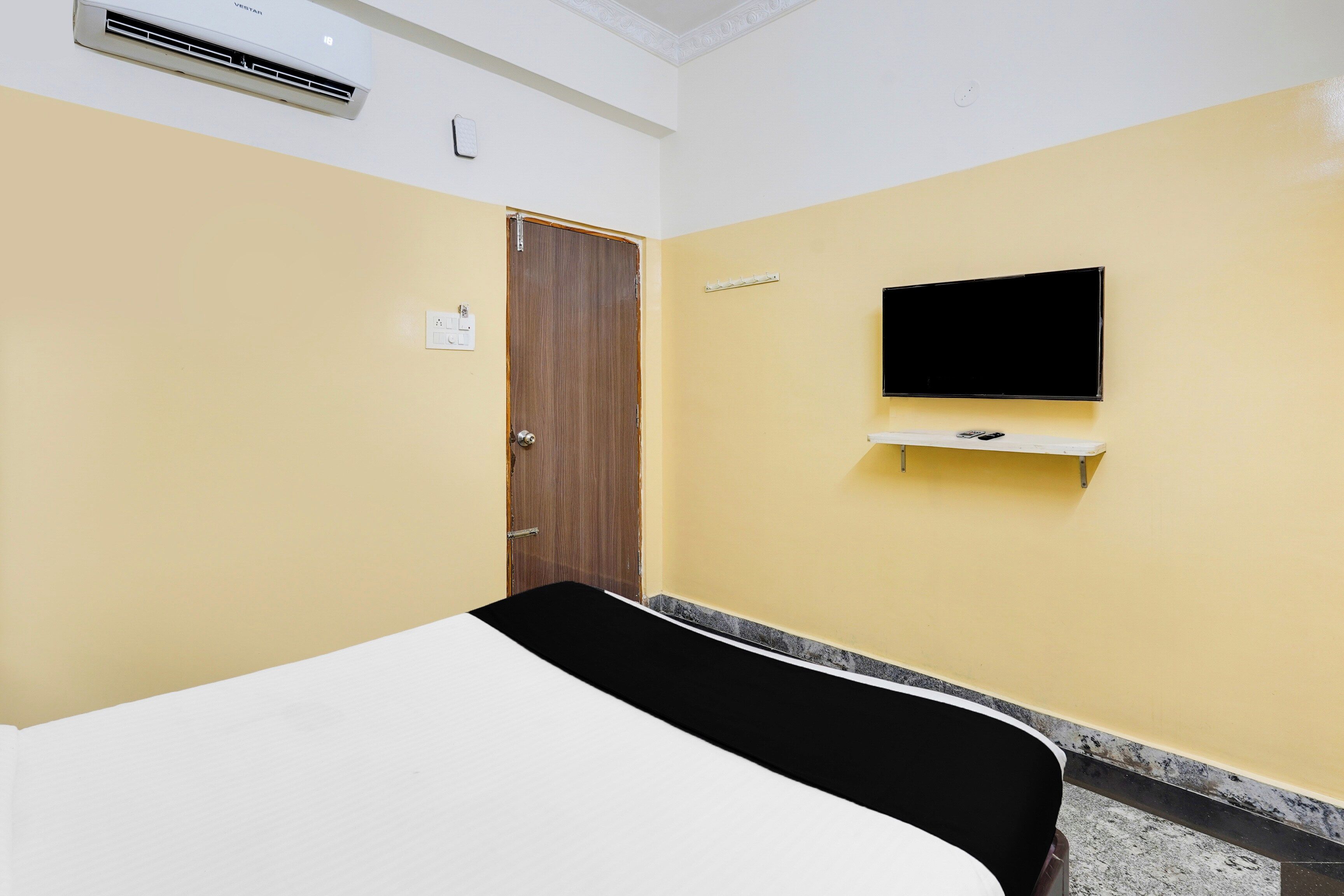 Quarto de hotel com cama, televisão fixada na parede e porta.