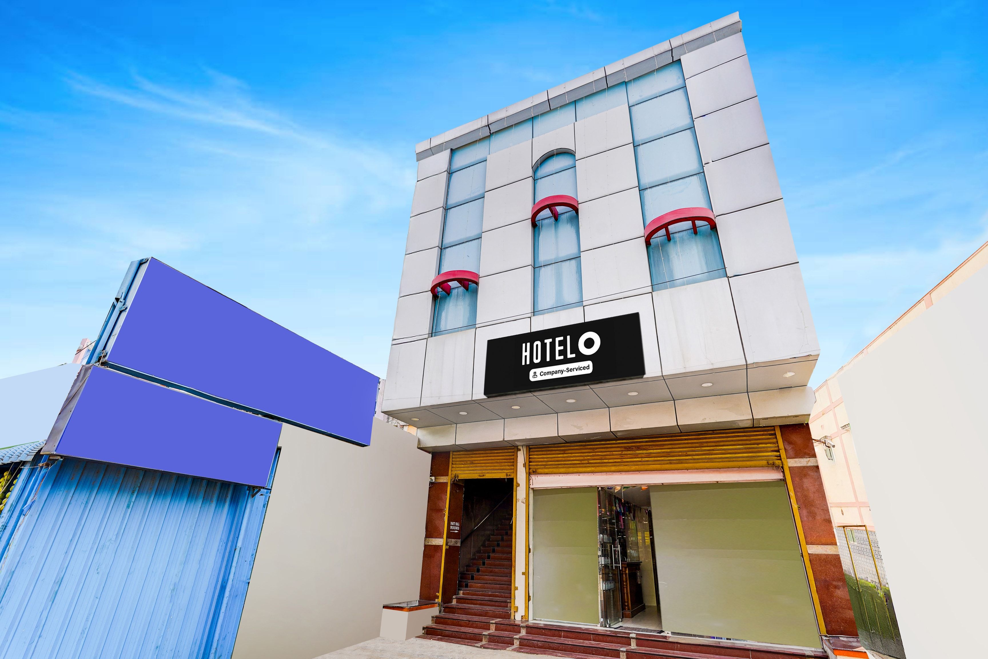 Um hotel com placa indicando serviço corporativo, uma escadaria que leva à entrada e um céu azul claro ao fundo.