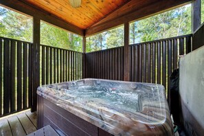 Banheira de hidromassagem numa área de deck de madeira com vista para árvores.