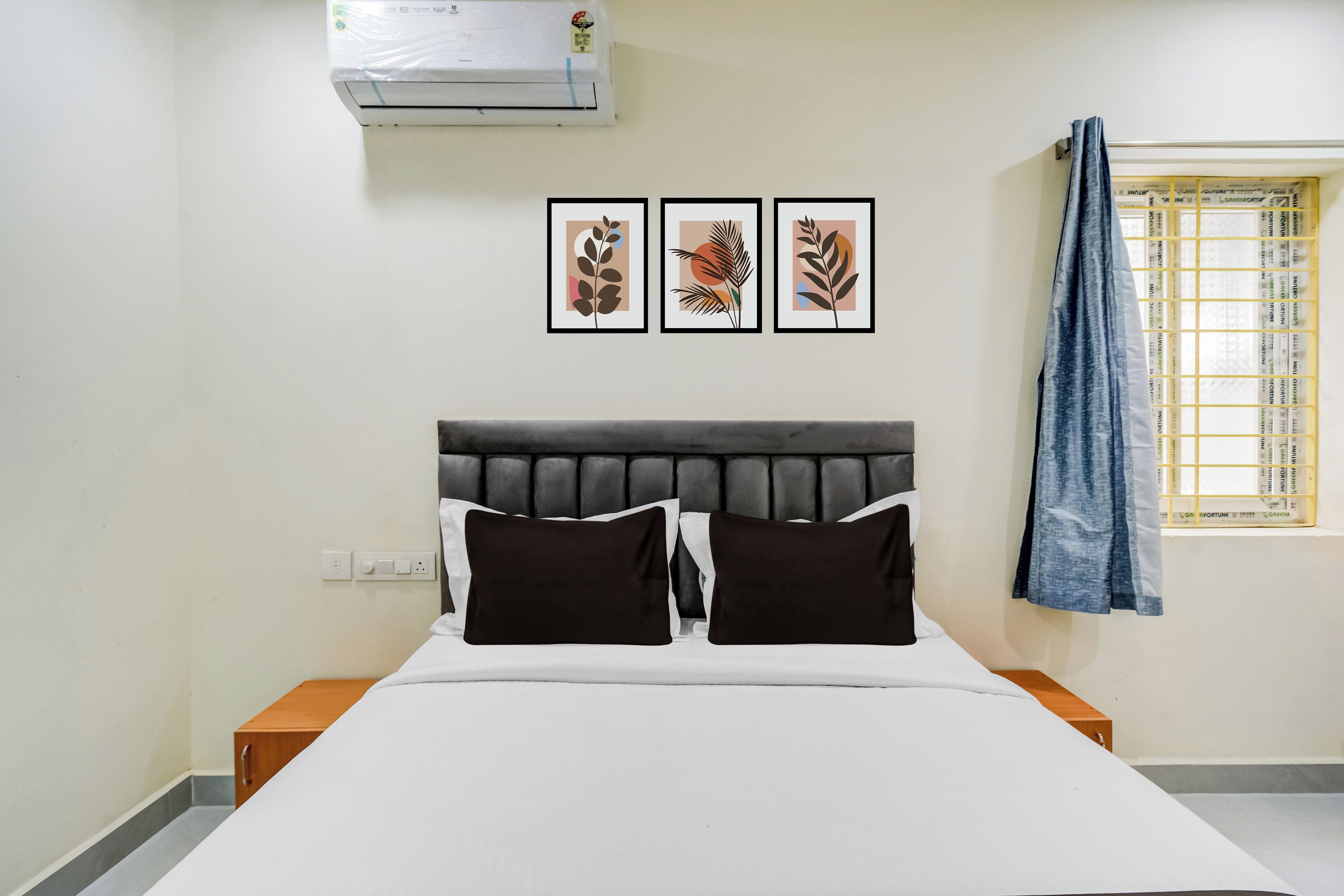 Quarto com cama, cabeceira, ar-condicionado fixado na parede e três obras de arte emolduradas.