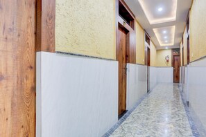 Corredor de hotel com painéis de madeira, paredes brancas e chão de mármore.