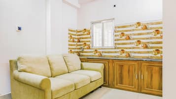 Sala de estar com sofá e área de cozinha, com armários de madeira e janela.