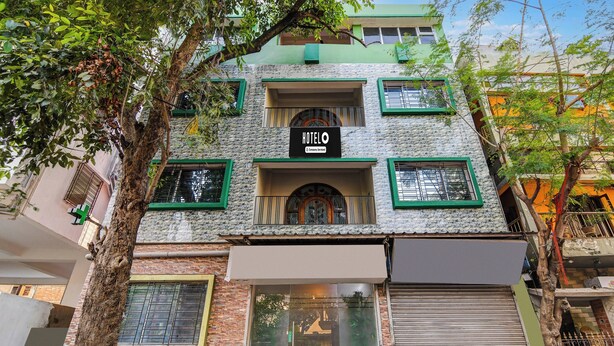 Um edifício com placa indicando ser um hotel, fachada de pedra, várias janelas com molduras verdes e entrada visível.