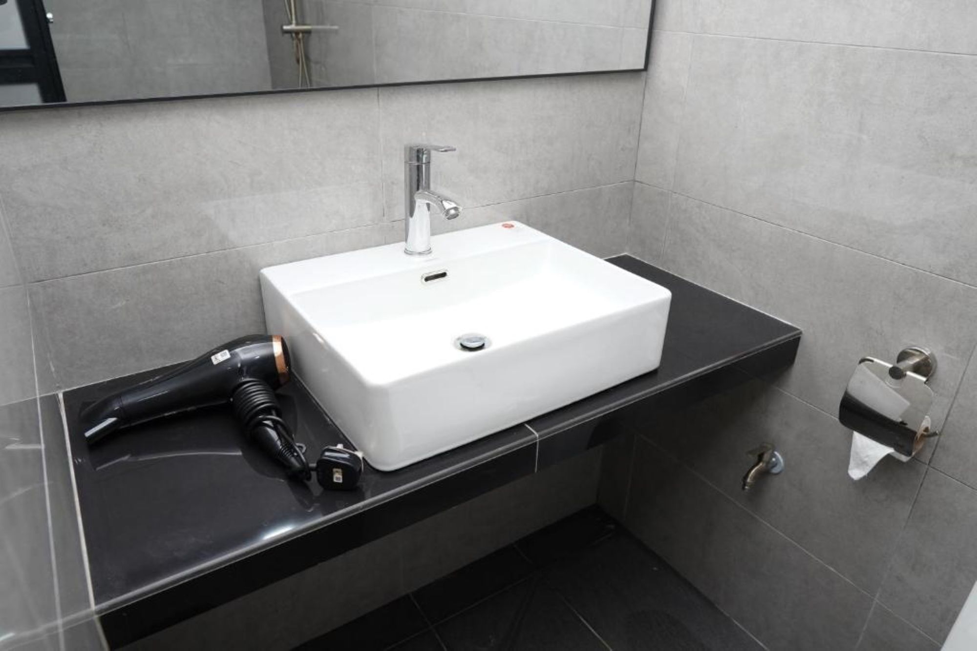 Casa de banho moderna com lavatório branco, bancada preta e espelho acima.