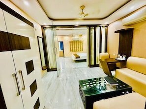 Quarto de hotel moderno com divisória de vidro, cama, sofá, mesa de centro e escrivaninha com luminária.