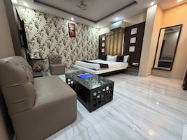 Uma sala de estar moderna com sofá, mesa de centro de vidro, cama com cabeceira e parede estampada.