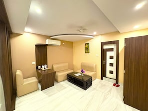 Quarto de hotel com sofá, mesa de centro, ar condicionado e uma porta.