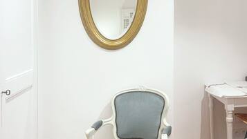 Quarto com porta branca, espelho, cadeira e cama com colcha florida.