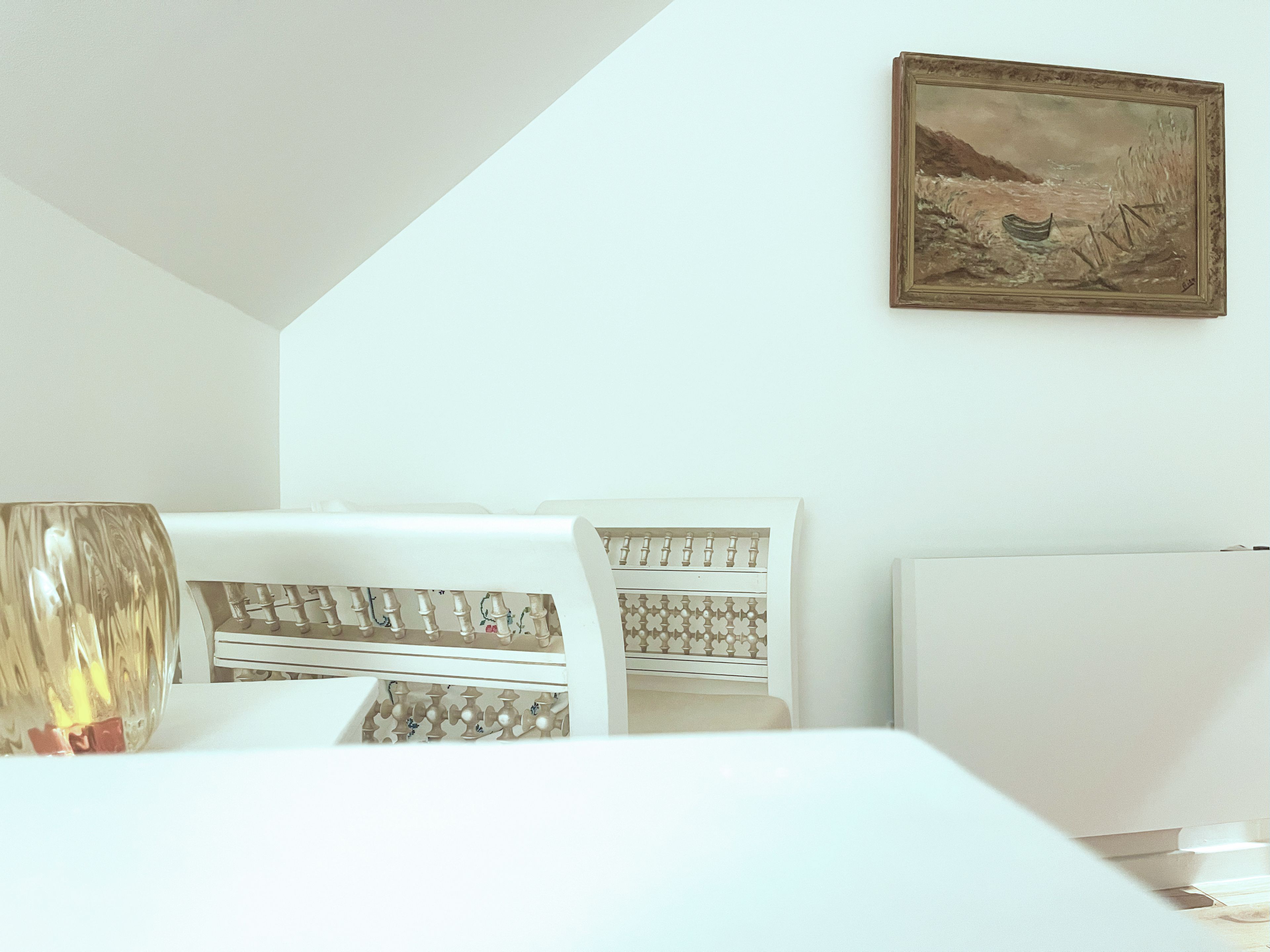 Quarto com cama branca, quadro emoldurado e papel de parede estampado.