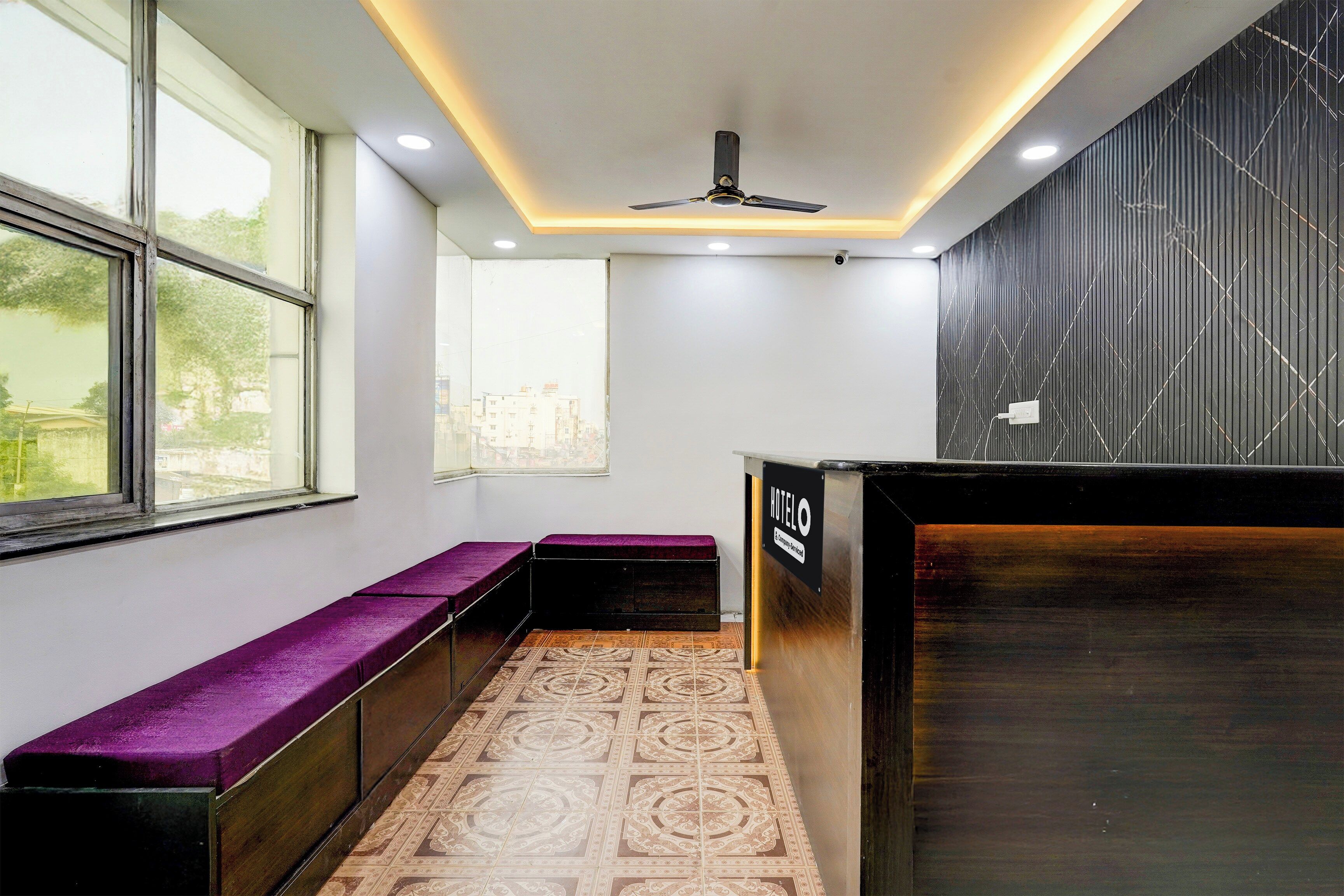 Uma área de recepção de hotel com balcão, espaço de estar com bancos e piso estampado.