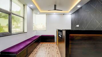 Uma área de recepção de hotel com balcão, espaço de estar com bancos e piso estampado.