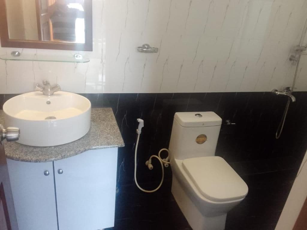 Casa de banho com lavatório branco, sanita e estante de vidro sobre o lavatório.