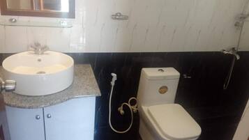 Casa de banho com lavatório branco, sanita e estante de vidro sobre o lavatório.